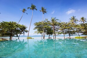 Piscina azul límpida rodeada por palmeiras e vista para o mar.