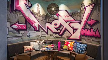 Uma área de lounge moderna com uma mesa de vidro, assentos confortáveis e um mural de graffiti vibrante na parede.