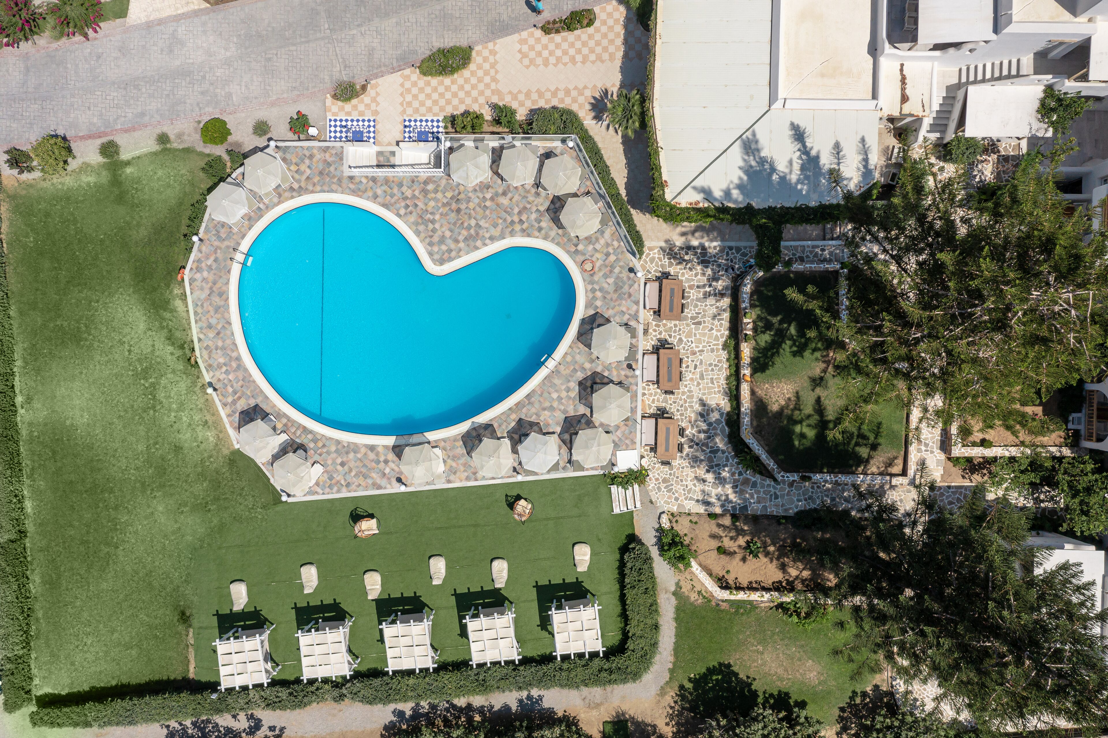 Vista aérea de uma propriedade com piscina em formato de coração, rodeada por espreguiçadeiras e guarda-sóis.