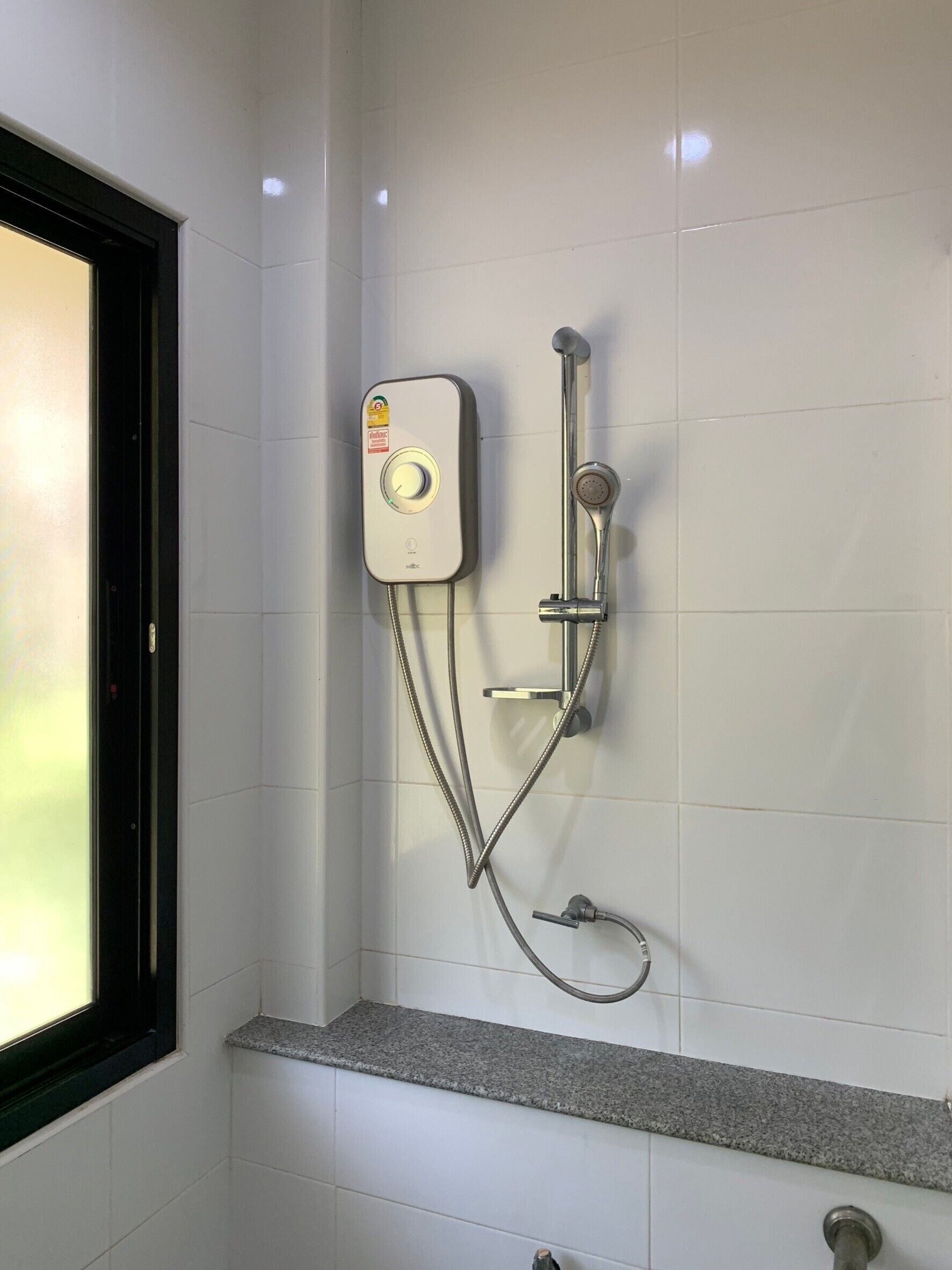 Chuveiro com painel de controle e chuveiro manual fixado em parede revestida com azulejos.