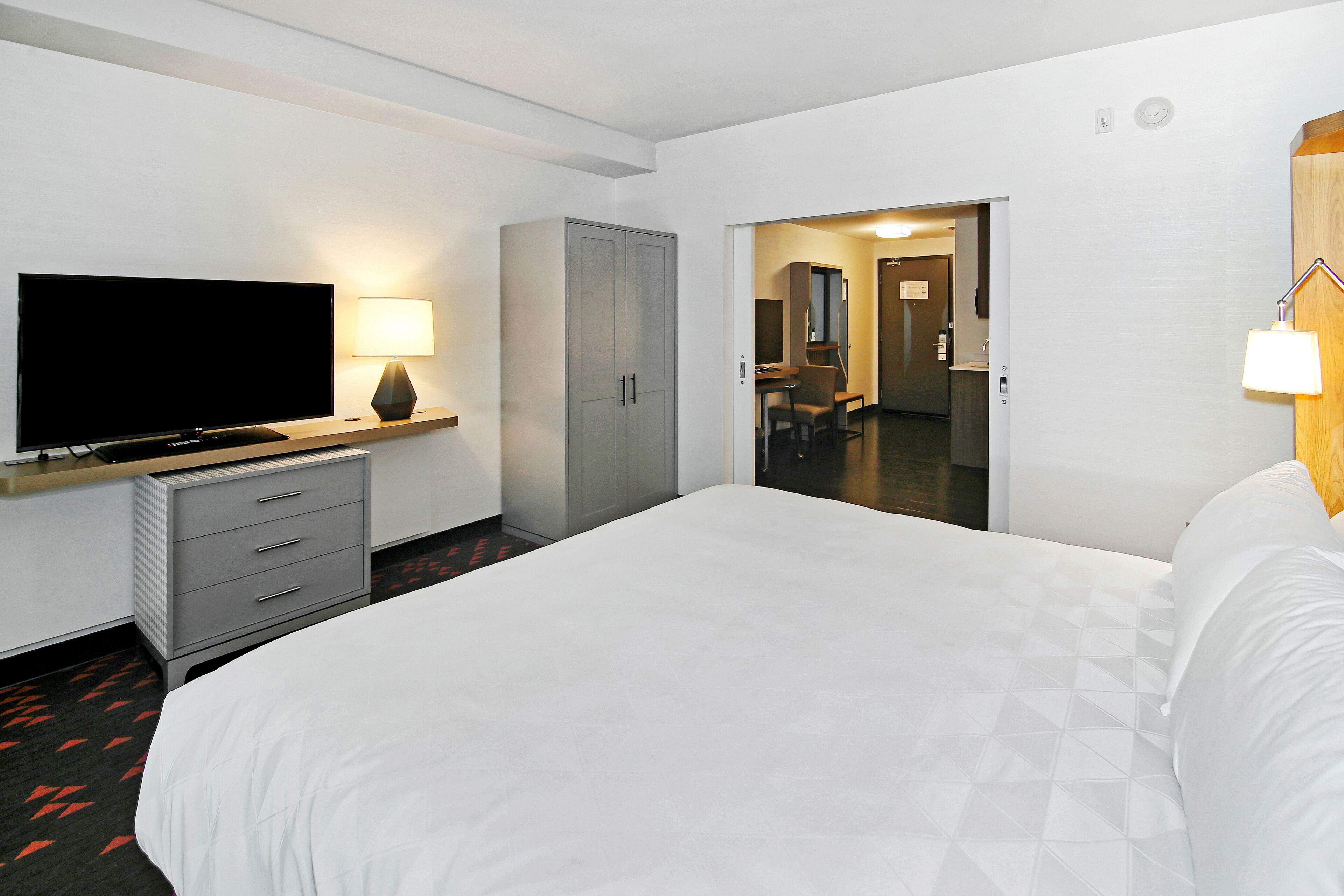 Quarto de hotel com cama, televisão, escrivaninha e guarda-roupa.