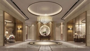 Um hall amplo com um lustre circular central, uma parede decorativa com uma planta e um tapete estampado.