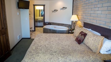 Quarto de hotel com uma cama grande, área de estar, banheiro com banheira e televisão fixada na parede.