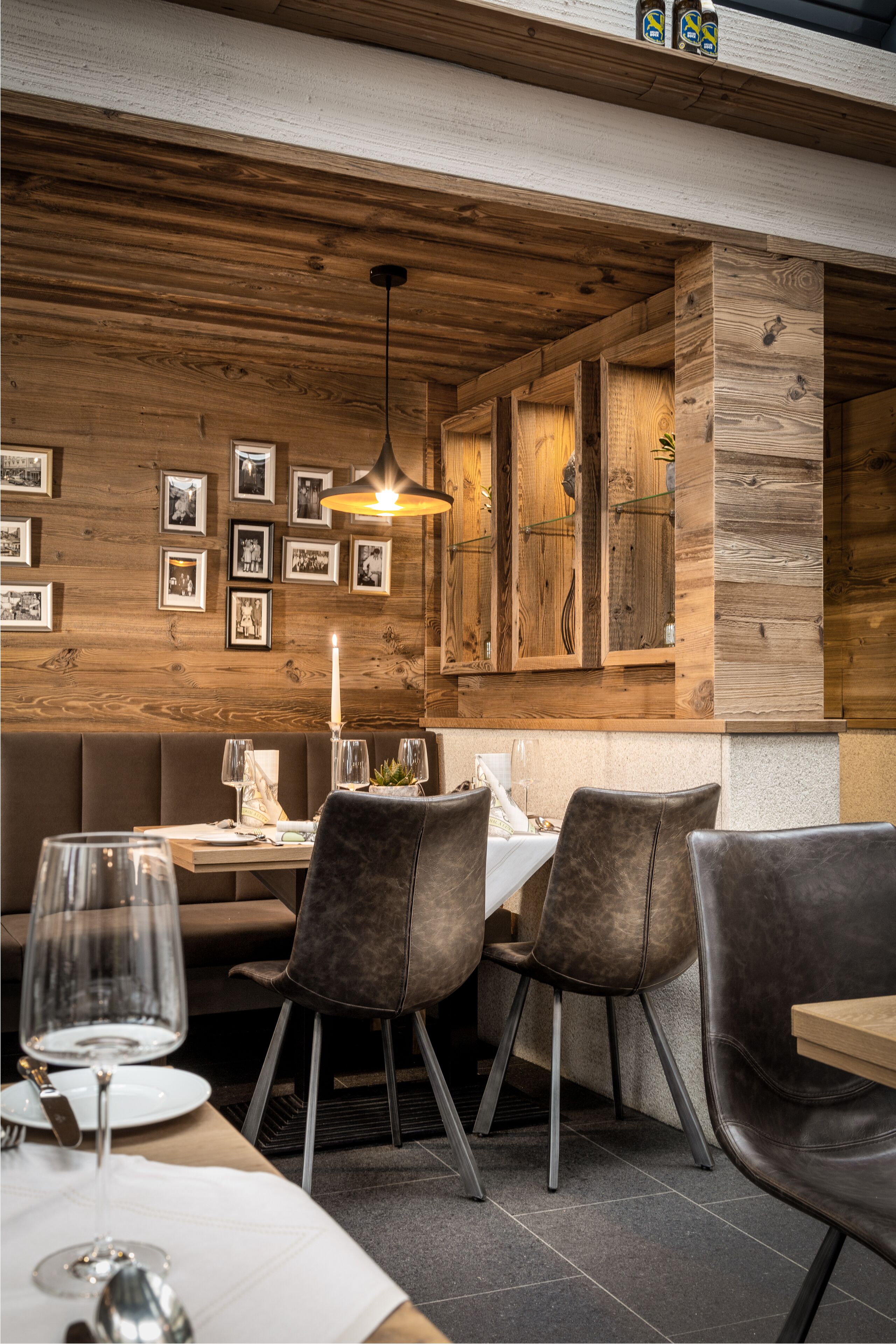 Restaurante com paredes de madeira, quadros decorativos e um moderno espaço de refeições com cadeiras de couro e um arranjo de velas.