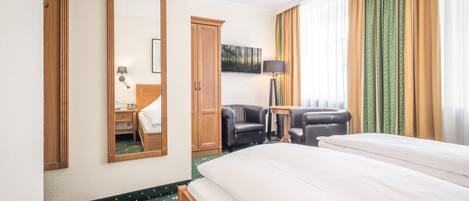 Quarto de hotel com uma cama grande, uma escrivaninha com cadeira, um guarda-roupa e um espelho.