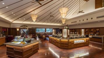 Um hall de hotel espaçoso com um bar central em ilha, piso de madeira, ventiladores de teto e uma grande janela que proporciona luz natural.