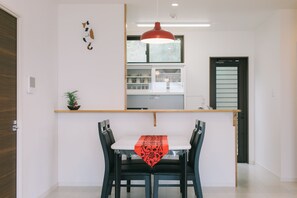 Uma área de refeições com mesa, cadeiras, um lustre, um vaso de planta e um armário com louças.