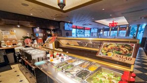 Uma área de buffet com diversas opções de comida, incluindo um canto de saladas e um balcão com temperos e utensílios.