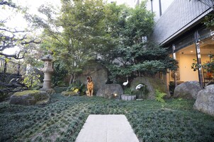 Um jardim com um candeeiro de pedra, pedras grandes e um caminho que leva a um edifício.