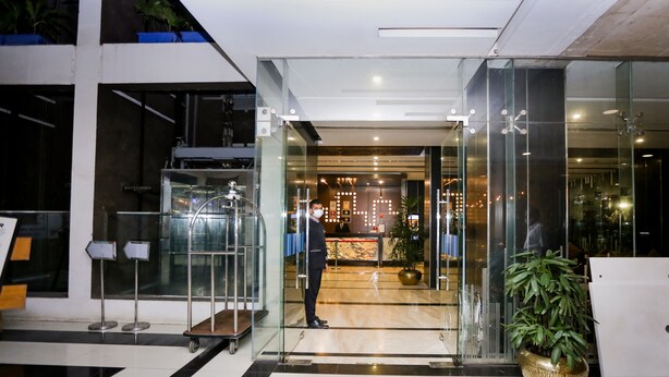 Um lobby de hotel moderno com um balcão de recepção, um elevador de vidro e uma planta em vaso.