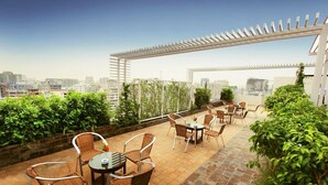 Terraço no telhado com área de estar externa, pérgola e vista para a cidade.