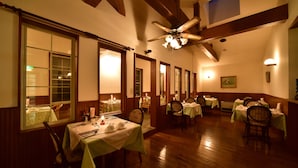 Um restaurante com vigas de madeira, várias mesas com toalhas verdes e um ventilador de teto.