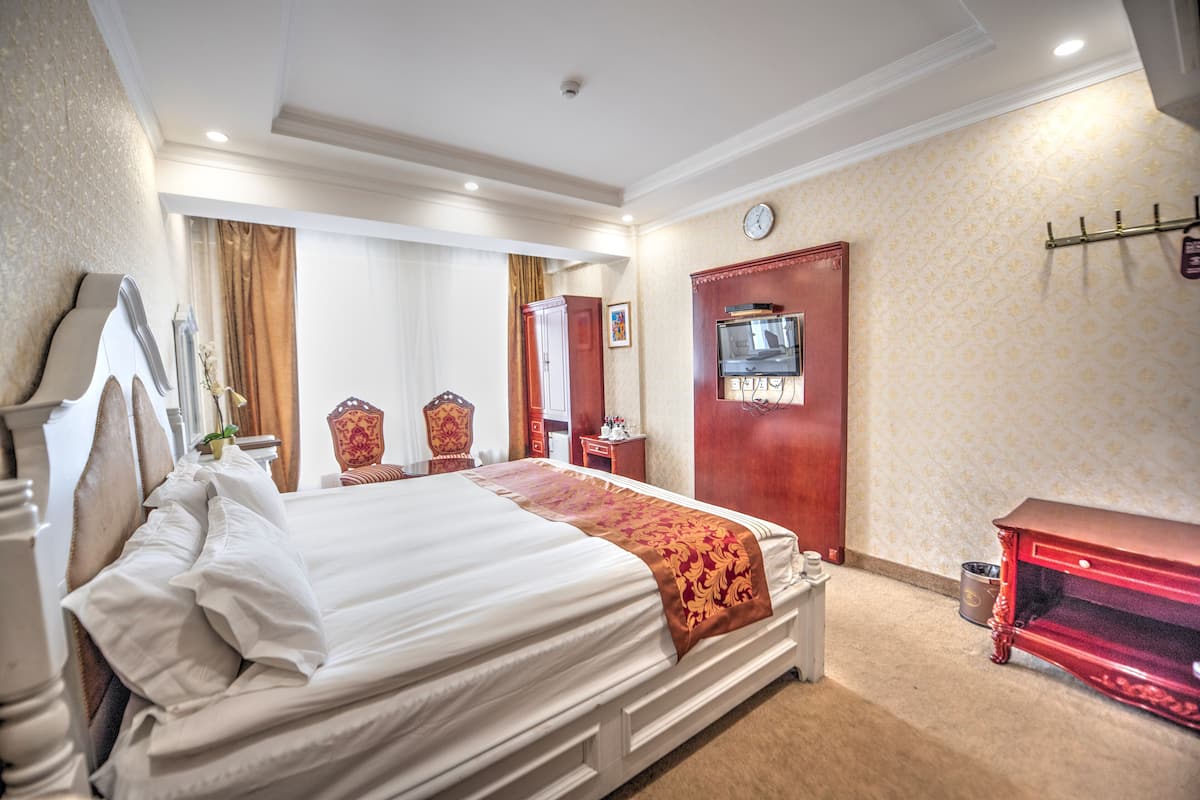 Quarto de hotel com uma cama grande, uma cômoda de madeira, uma televisão e um relógio na parede.