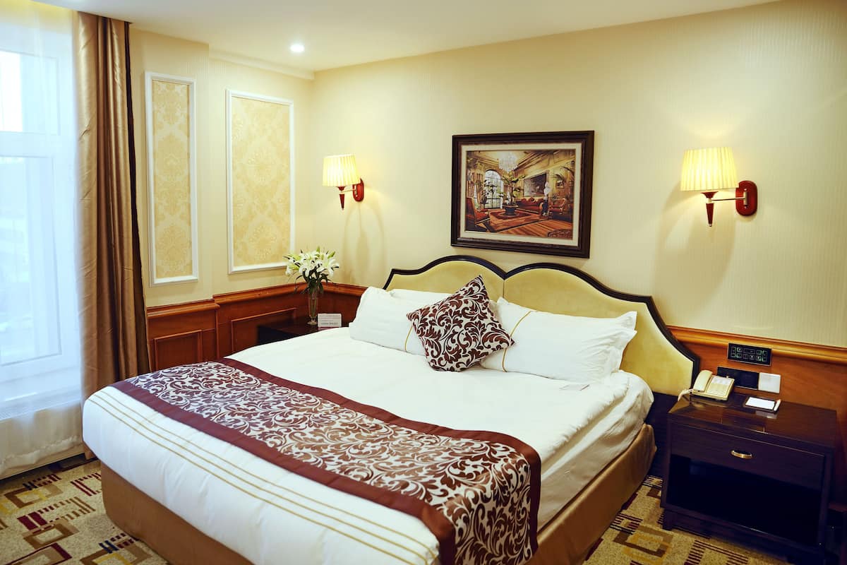 Quarto de hotel com uma cama grande, uma mesa de cabeceira com telefone e um quadro na parede.