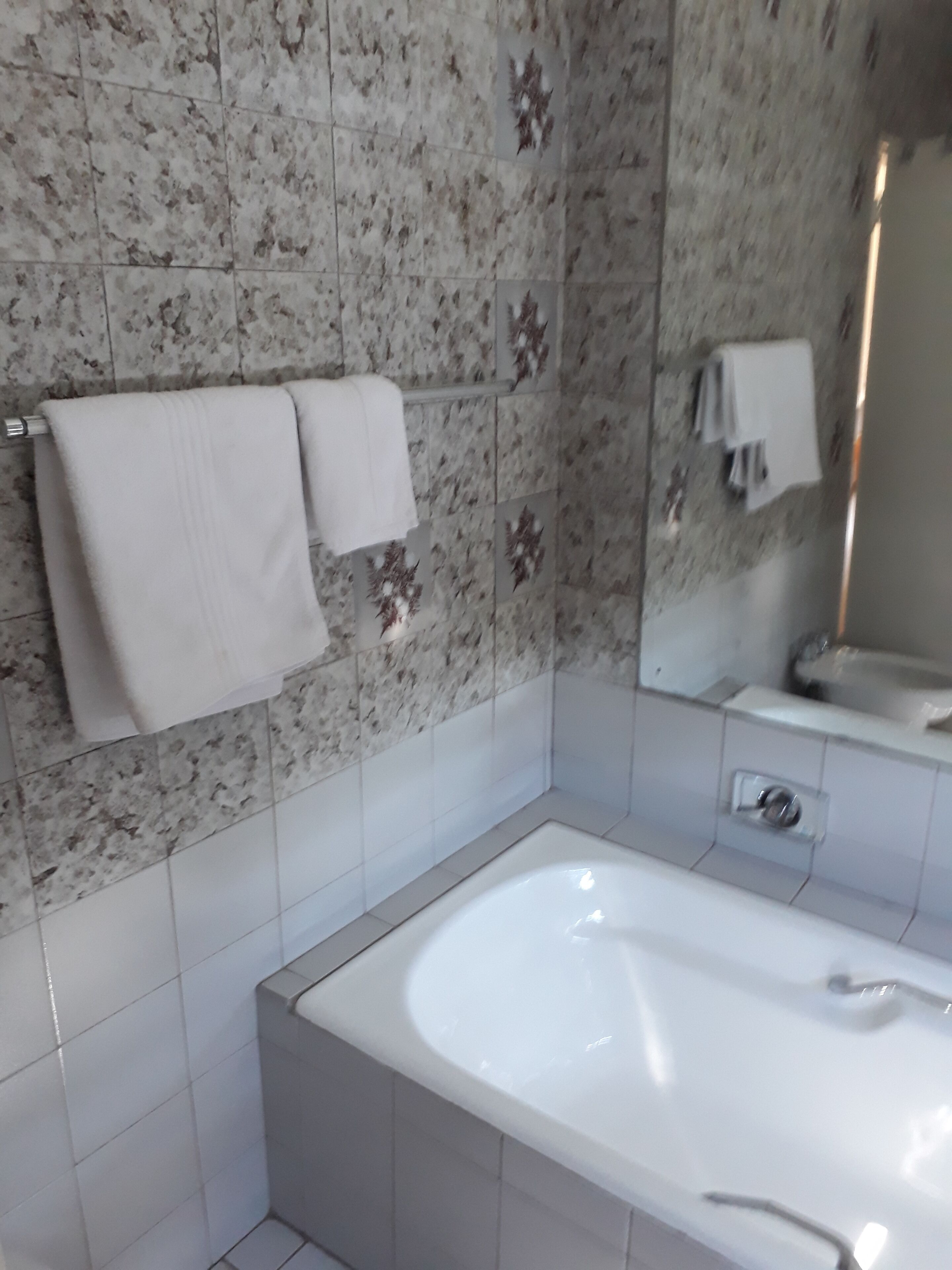 Um banheiro com banheira branca, espelho e paredes revestidas de azulejos com padrão floral.