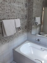 Um banheiro com banheira branca, espelho e paredes revestidas de azulejos com padrão floral.