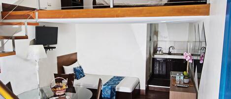 Quarto de hotel compacto com cama beliche, área de jantar com mesa de vidro e cozinha compacta.