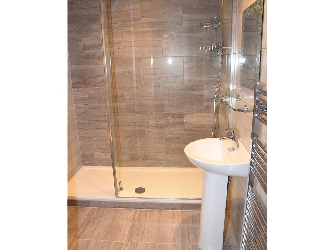 Casa de banho moderna com cabine de duche em vidro, lavatório pedestal branco e chão em mosaico.