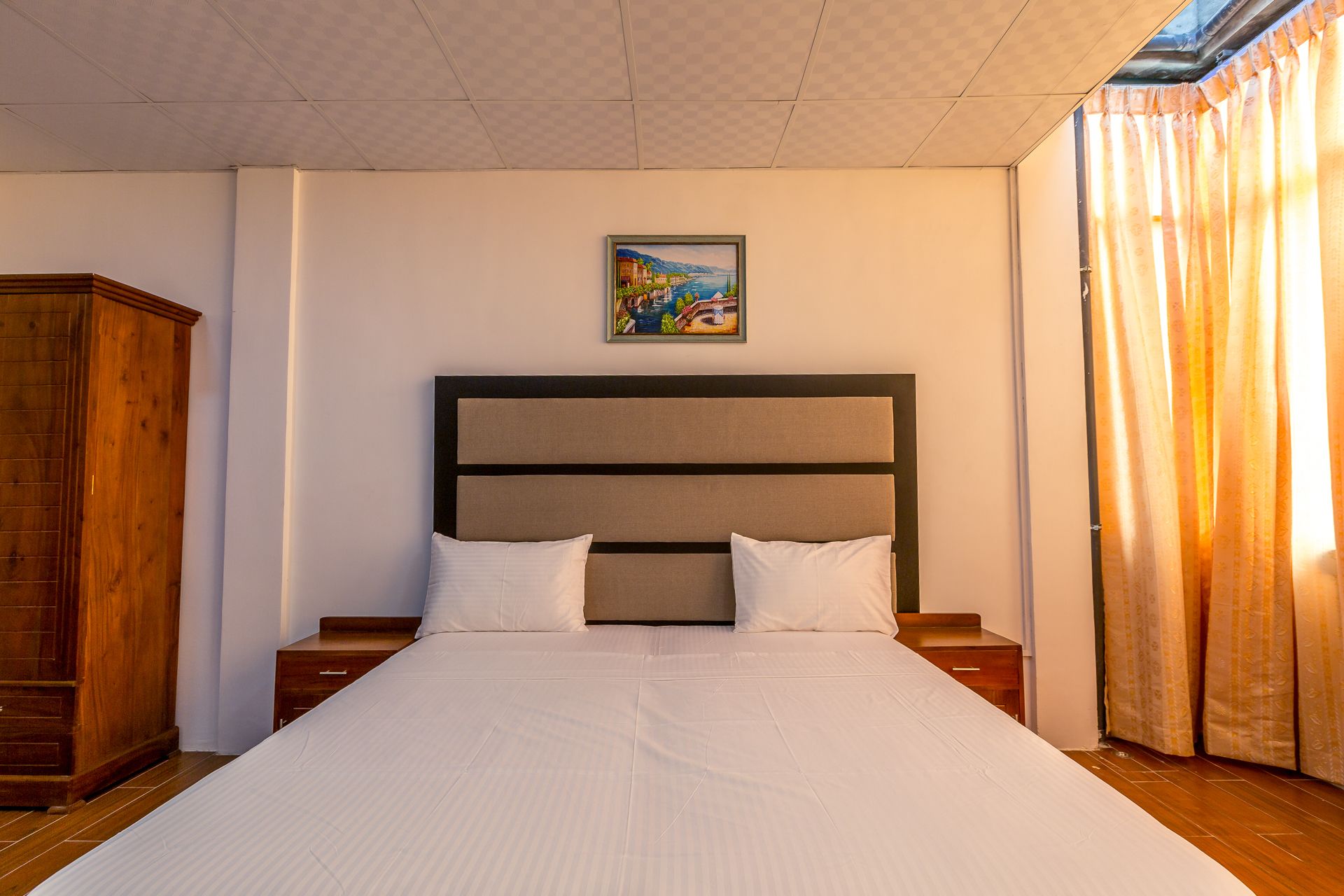 Quarto bem arrumado com uma cama grande, guarda-roupa de madeira e um quadro na parede.