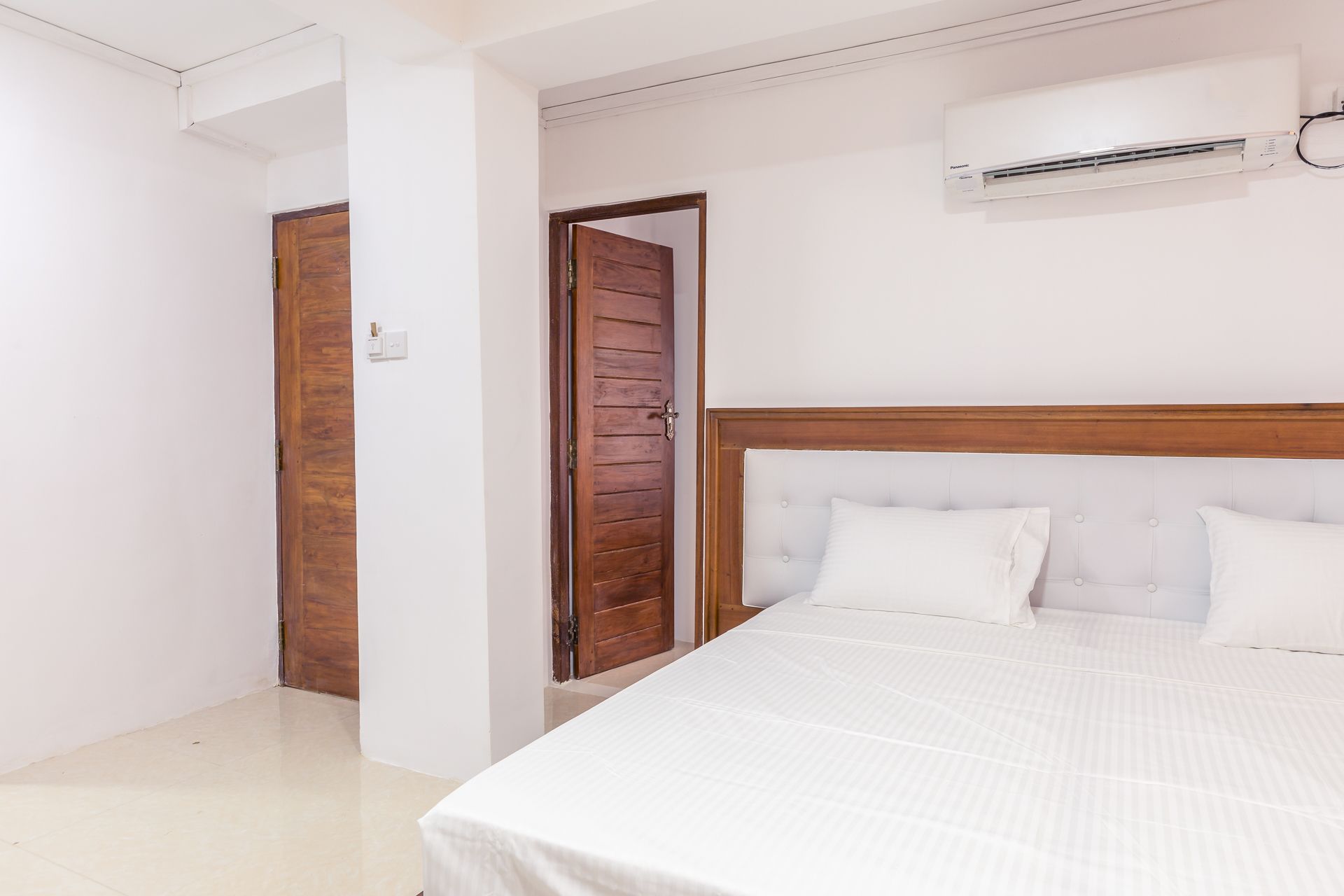 Quarto com cama, porta de madeira e ar condicionado.