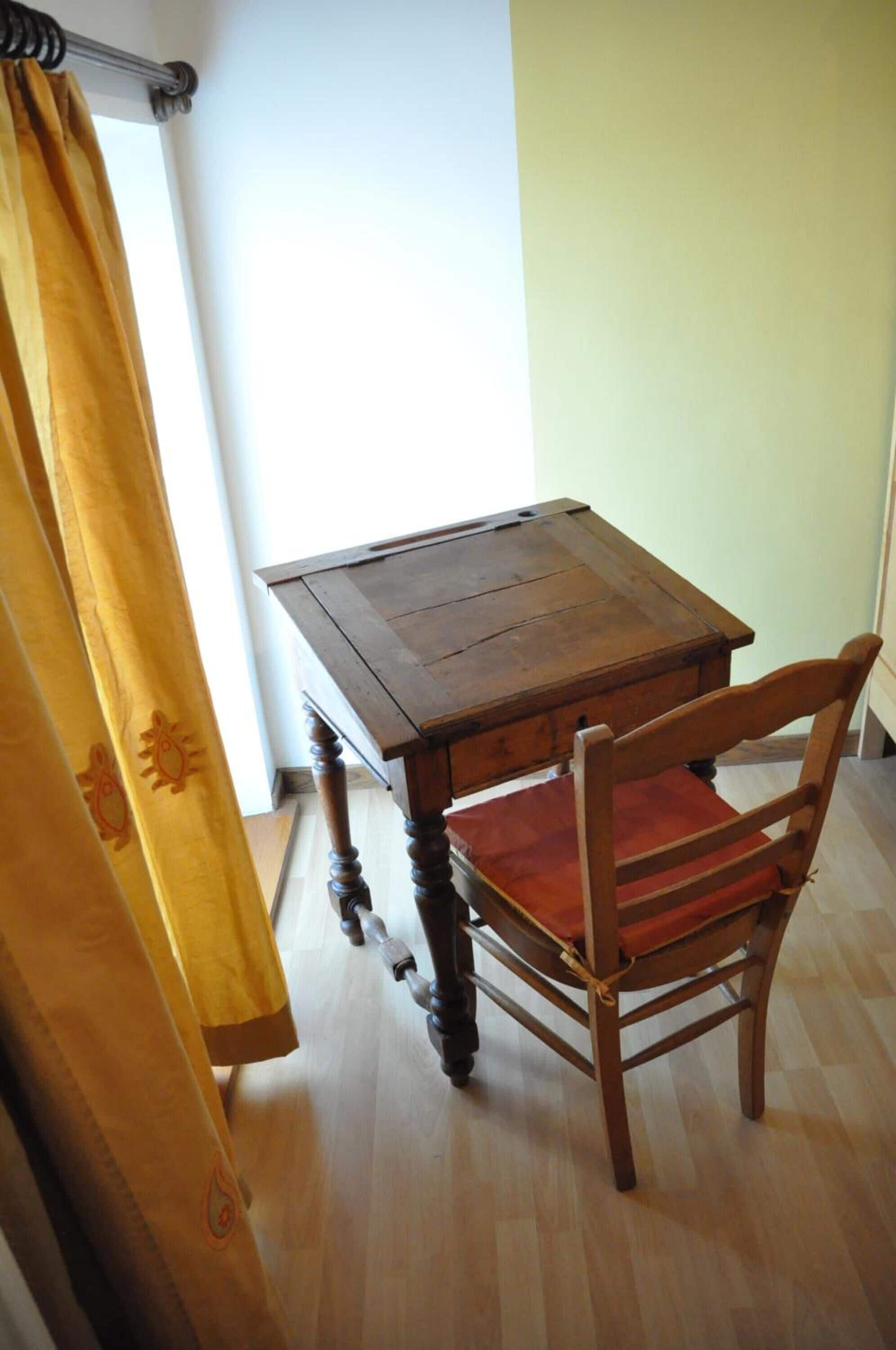 Uma mesa de madeira com uma cadeira, uma cortina com desenhos de sol e uma parede de cor clara.