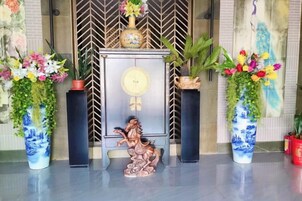 Uma área de recepção com um armário decorativo, uma estátua e plantas em vasos.