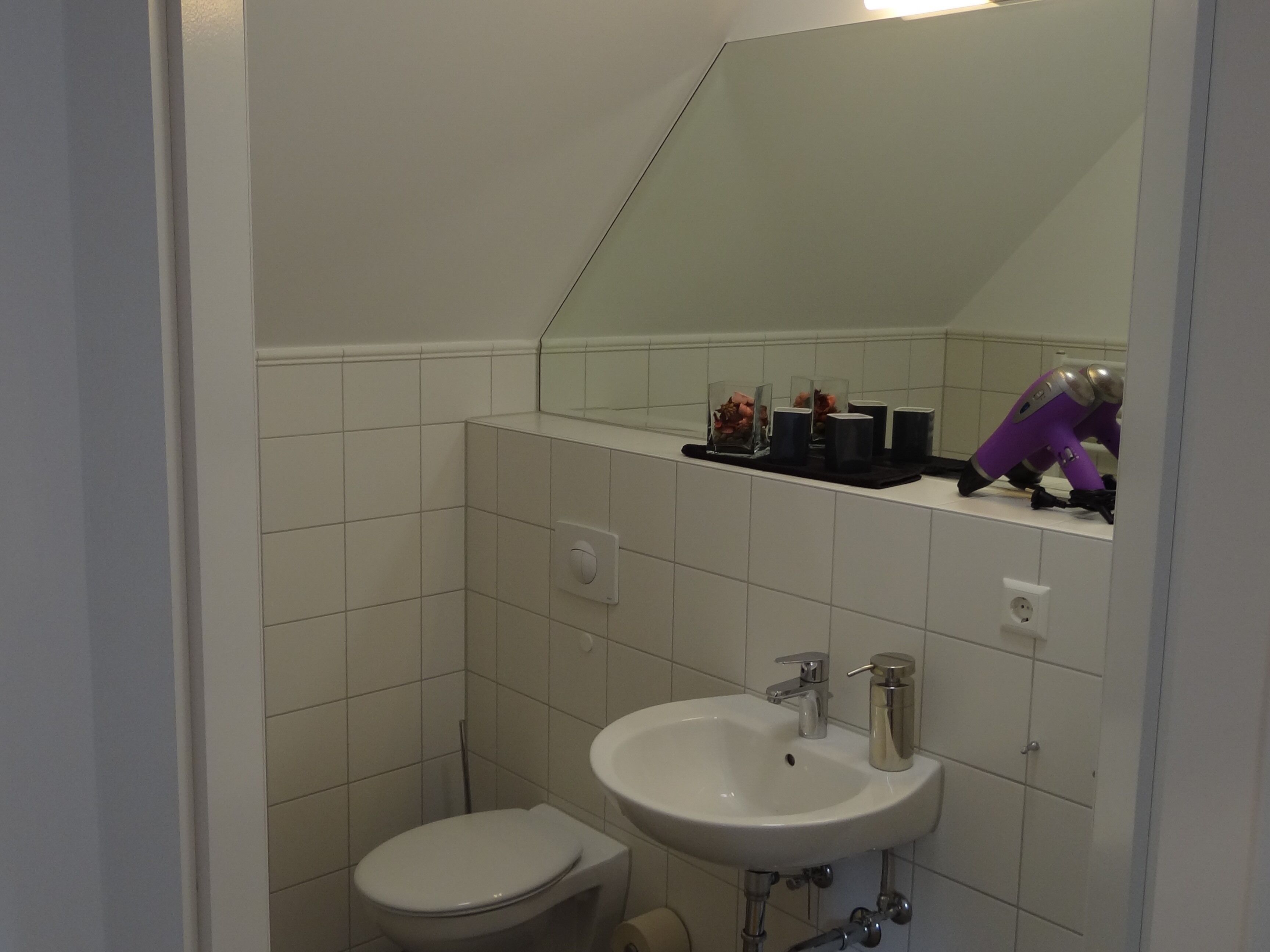 Um banheiro pequeno com vaso sanitário, pia e espelho. Há um secador de cabelo sobre o balcão.