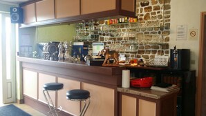 Uma área de bar com banquetas, uma parede de pedra, prateleiras com garrafas e um monitor de computador.