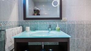 Casa de banho com lavatório de vidro, espelho e porta-toalhas.