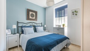Quarto com cama, mesas de cabeceira, janela com persianas e um quadro na parede.