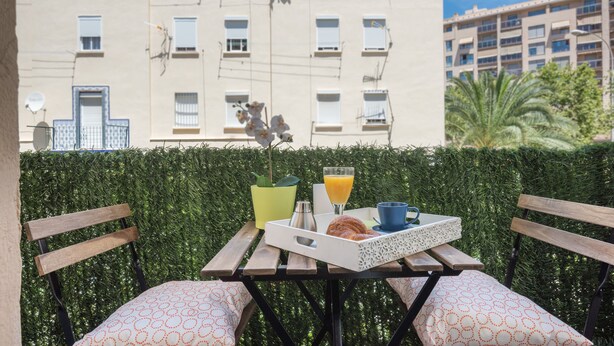 Mesa posta com itens de café da manhã, um banco e vista para um edifício com várias janelas e sacadas.