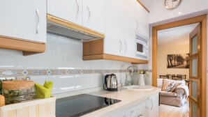 Uma cozinha moderna com armários brancos, forno embutido e micro-ondas. Há uma cafeteira, um bule e uma máquina de lavar.