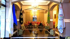 Um lobby luxuoso com um candelabro, sofás elaborados e bandeiras.