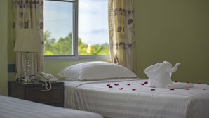 Quarto de hotel com uma cama, mesa de cabeceira com abajur e telefone, e uma janela com cortinas.