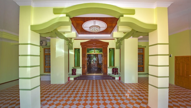 Um corredor com piso xadrez, pilares verdes e brancos e teto de madeira com lustre.