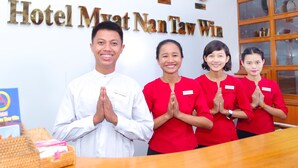 Um balcão de recepção com uma placa indicando "Hotel Myat Nan Taw Win" e relógios exibindo horários de diferentes países.