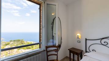 Quarto com vista para o mar, uma cadeira de madeira, uma mesa de cabeceira pequena e uma cama com cabeceira.