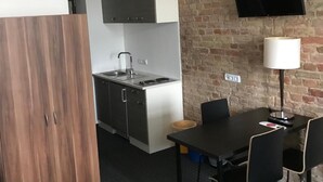 Quarto compacto com cozinha compacta, mesa de jantar com cadeiras, TV presa em uma parede de tijolos e guarda-roupa de madeira.