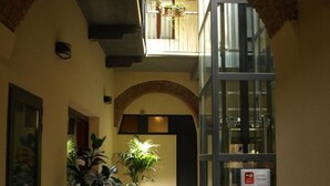 Um corredor estreito com um arco de tijolos, plantas em vasos e um eixo de elevador de vidro.