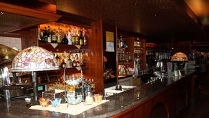 Uma área de bar com balcão de madeira, diversos frascos e uma luminária de vitral decorativa.