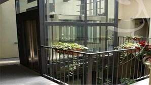 Uma varanda moderna com grades de metal, plantas em vasos e vista para o interior do edifício.