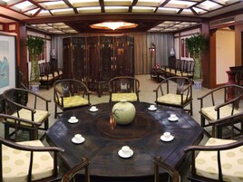 Uma sala de jantar em estilo tradicional com uma mesa redonda rodeada por cadeiras, um vaso grande no centro e plantas em vasos.