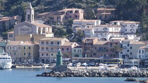 Uma cidade costeira com edifícios históricos, um farol e uma marina com barcos.
