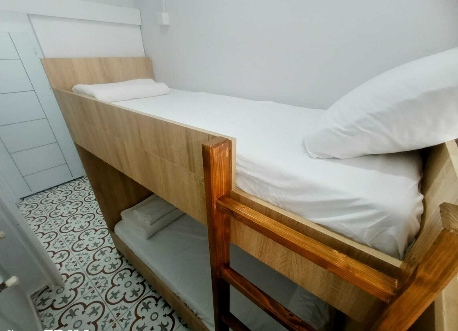 Uma cama de beliche com estrutura de madeira e roupa de cama branca em um quarto com ladrilhos estampados.