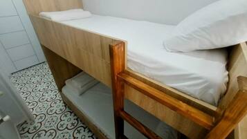 Uma cama de beliche com estrutura de madeira e roupa de cama branca em um quarto com ladrilhos estampados.