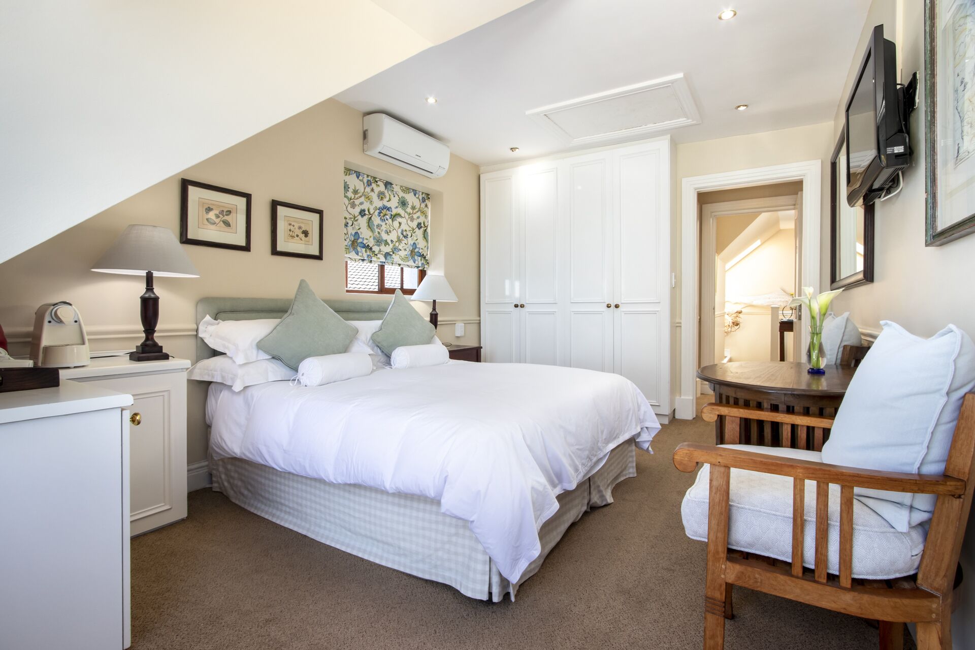 Quarto com cama, mesas de cabeceira, escrivaninha, cadeira, espelho e porta.