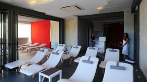 Uma área de spa moderna com espreguiçadeiras brancas, uma parede de destaque vermelha e teto com design exclusivo.