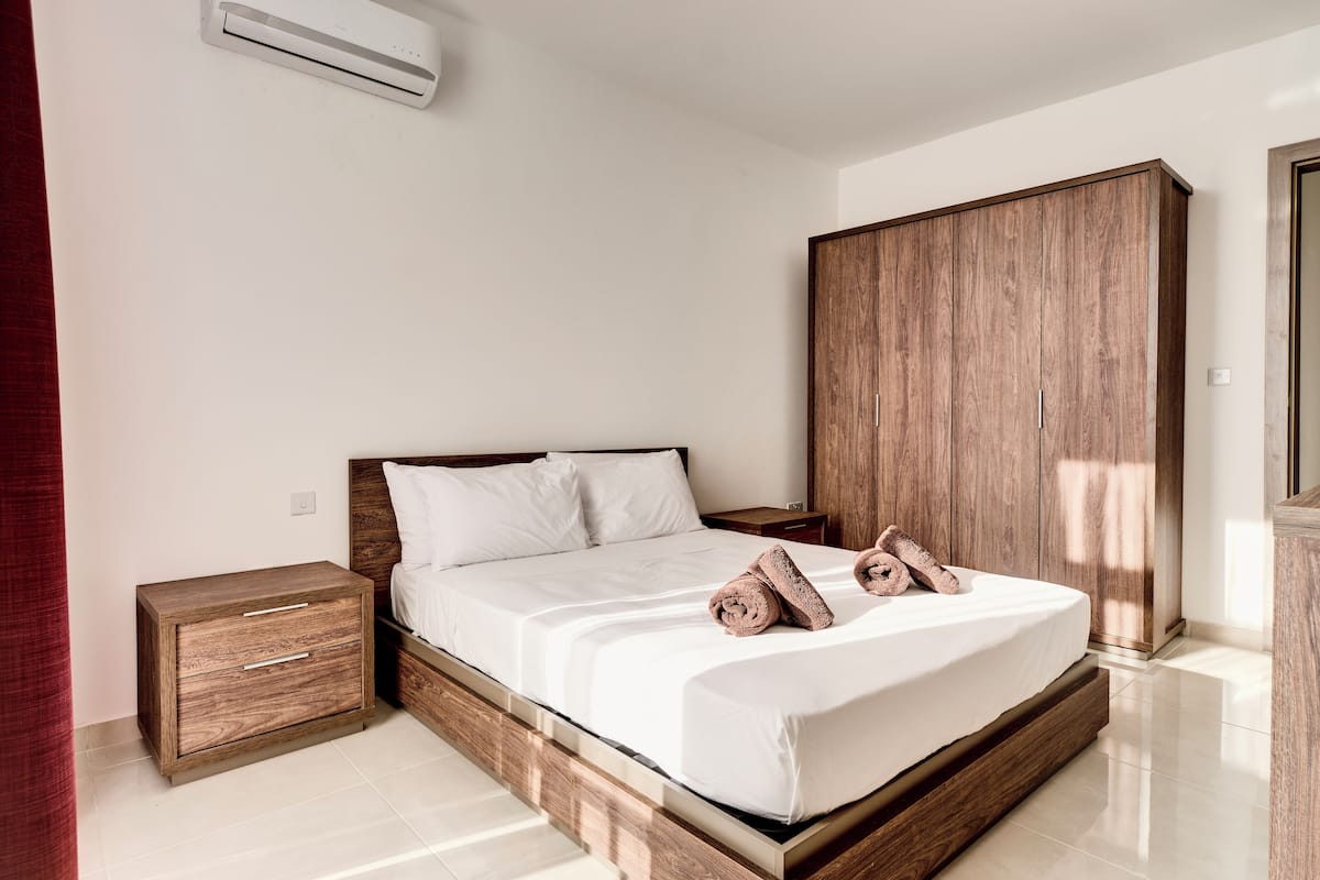 Quarto moderno com estrutura de cama de madeira, roupa de cama branca e guarda-roupa de madeira.