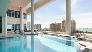 Uma piscina interior moderna com vista clara para o horizonte da cidade, grandes janelas e uma área de lounge ampla.