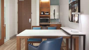 Quarto de hotel pequeno com uma mesa de jantar de madeira, cadeiras estofadas em azul, micro-ondas, máquina de café e sanita branca.